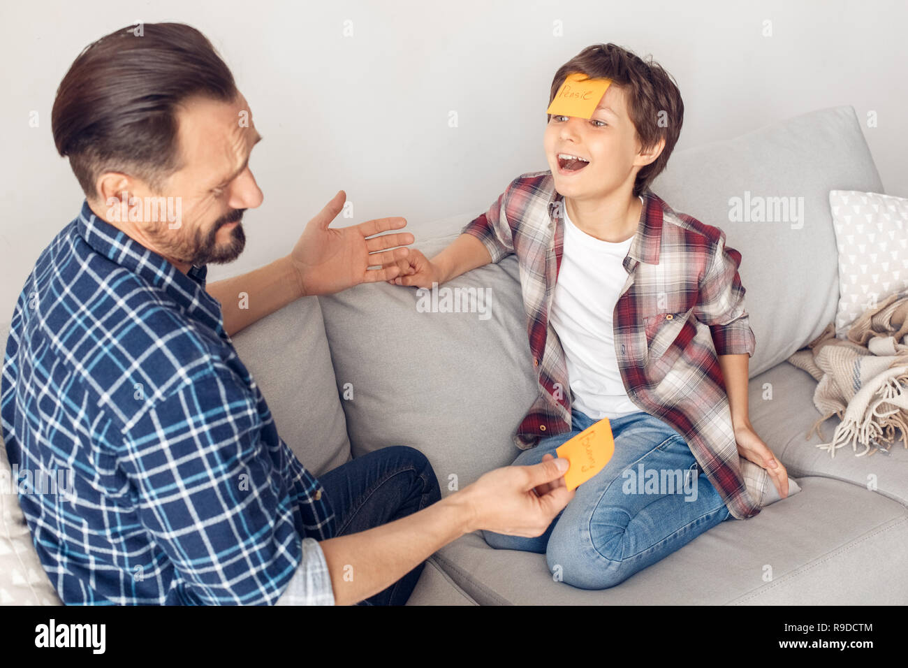 Father and little son together at home sitting on sofa playing forehead ...