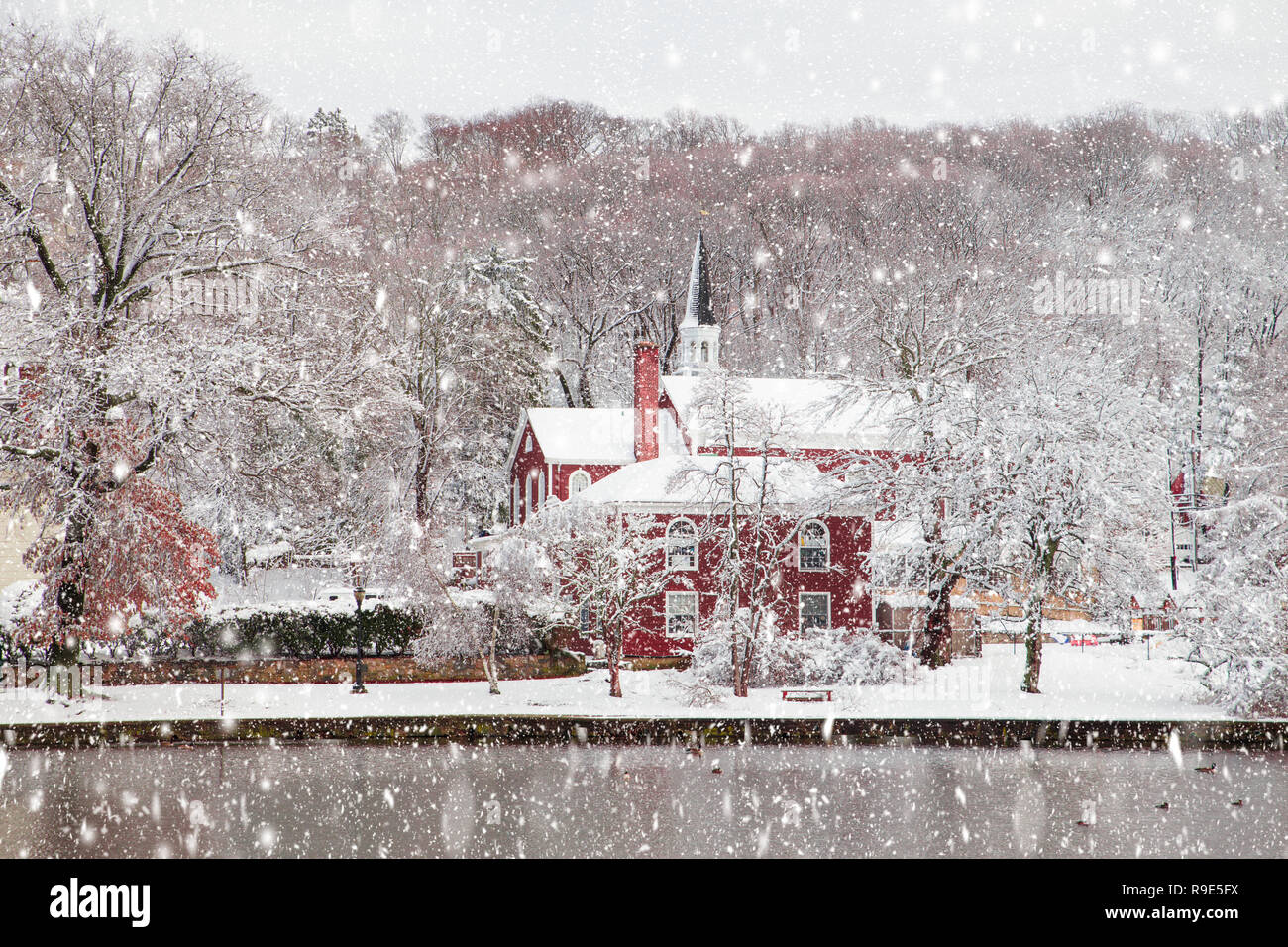 Beautiful rural winter scene with church, trees, pond with falling snow ...
