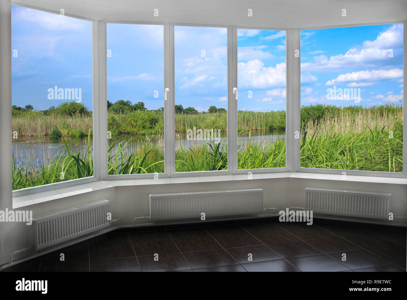 Room with wide window overlooking landscape with lake surrounded with ...