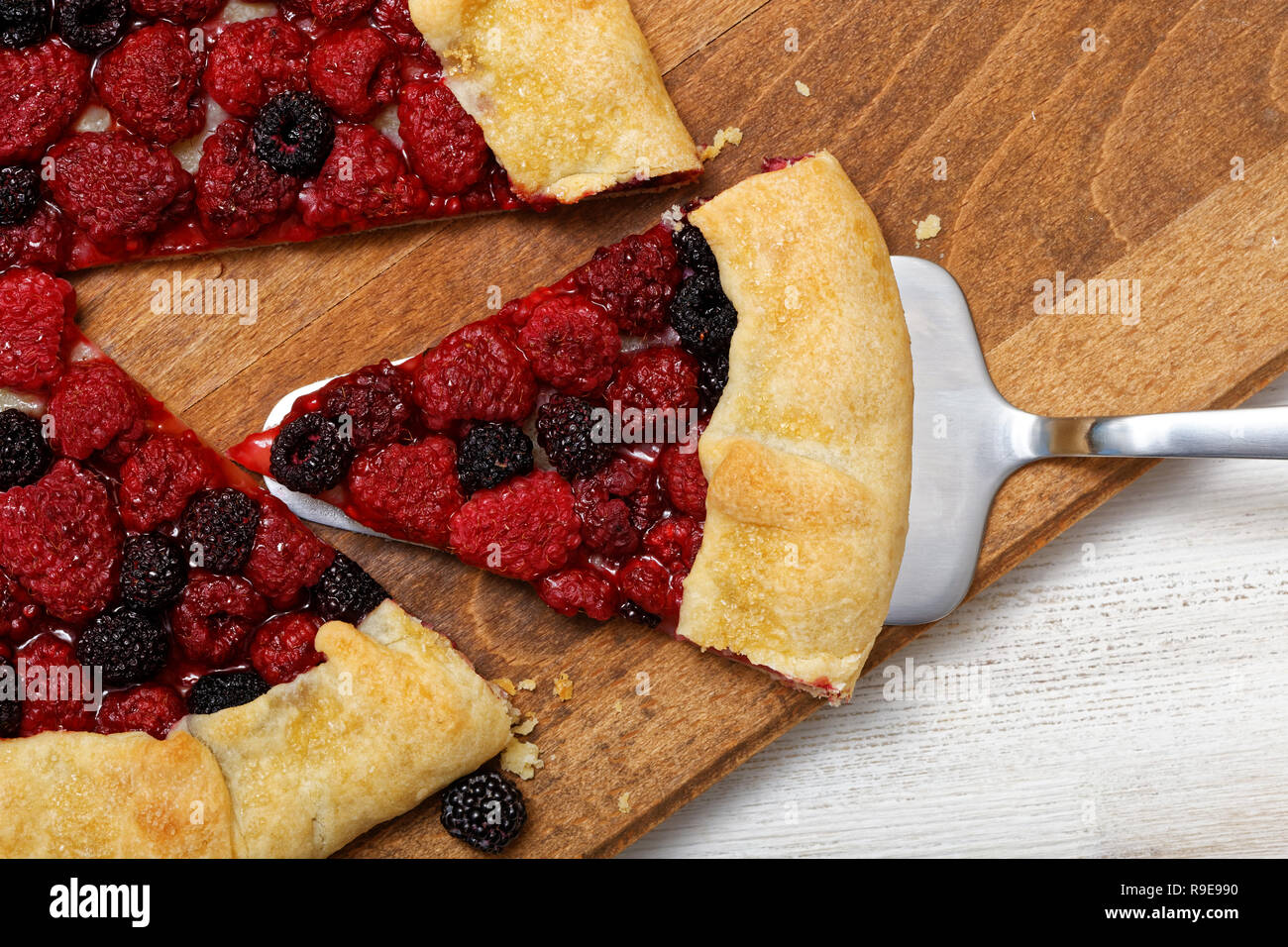 Homemade raspberries galette with a piece cut off on a wooden cutting ...