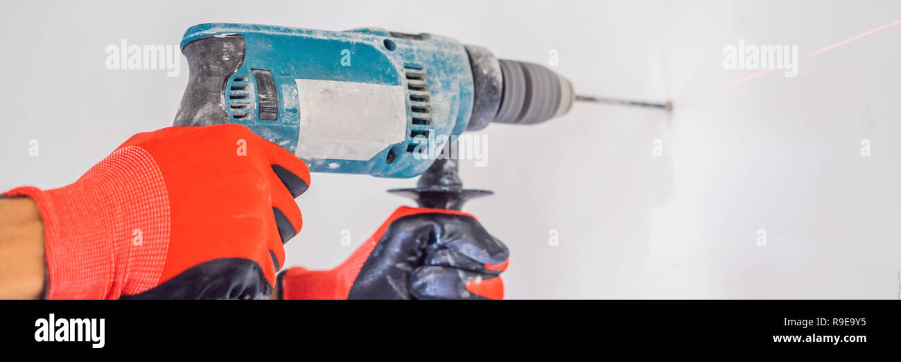 A man makes a hole in the wall with a drill BANNER, LONG FORMAT Stock ...
