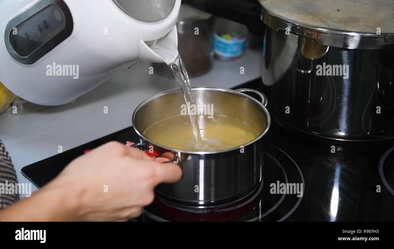 Caucasian woman pouring hot water into pot, cooking traditional soup ...