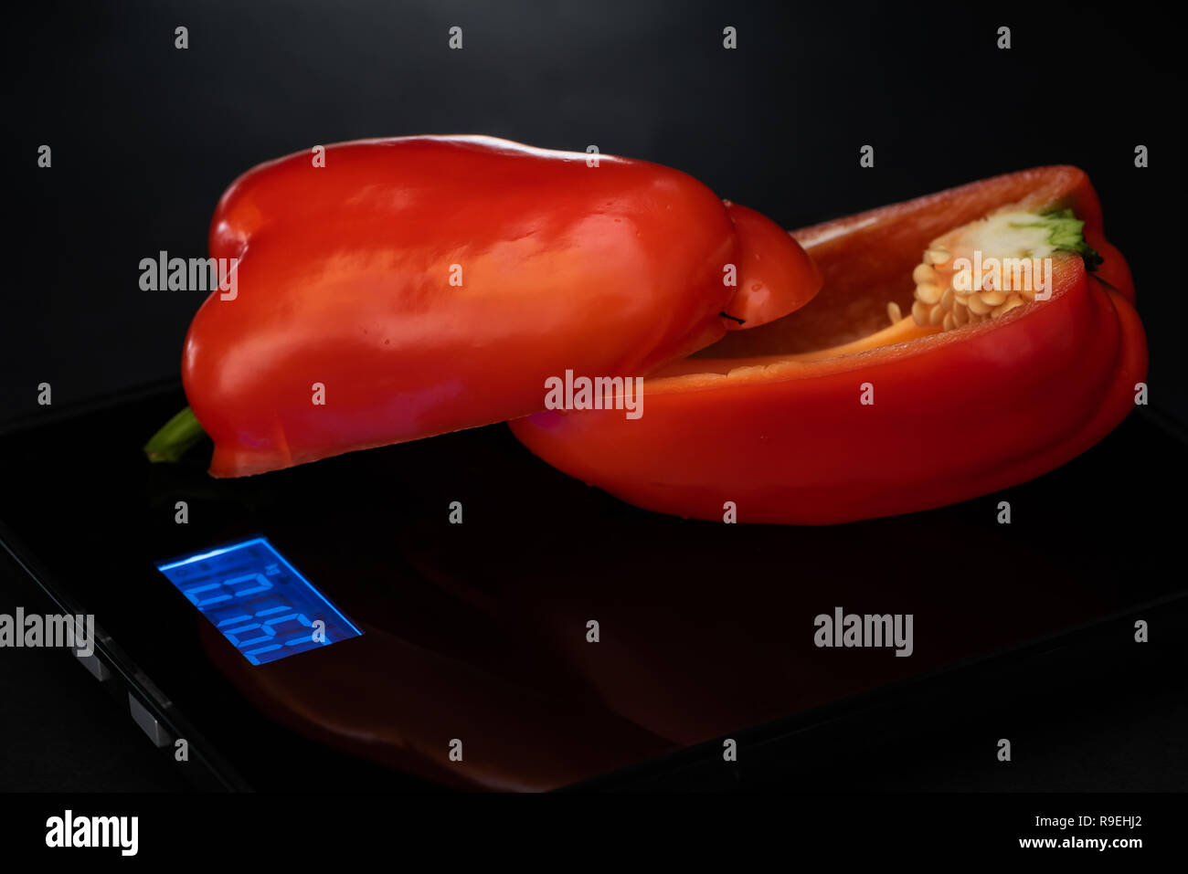 Cut in half red pepper is on an electronic weight on a black background ...
