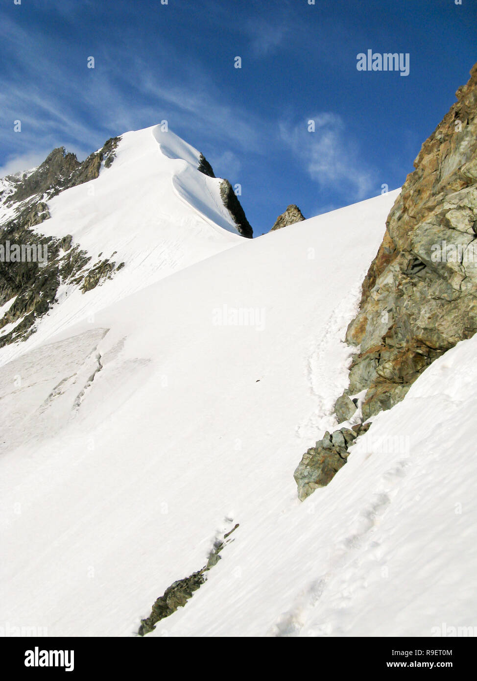 mountain climbers on a steep and narrow snow ridge leading to a high ...