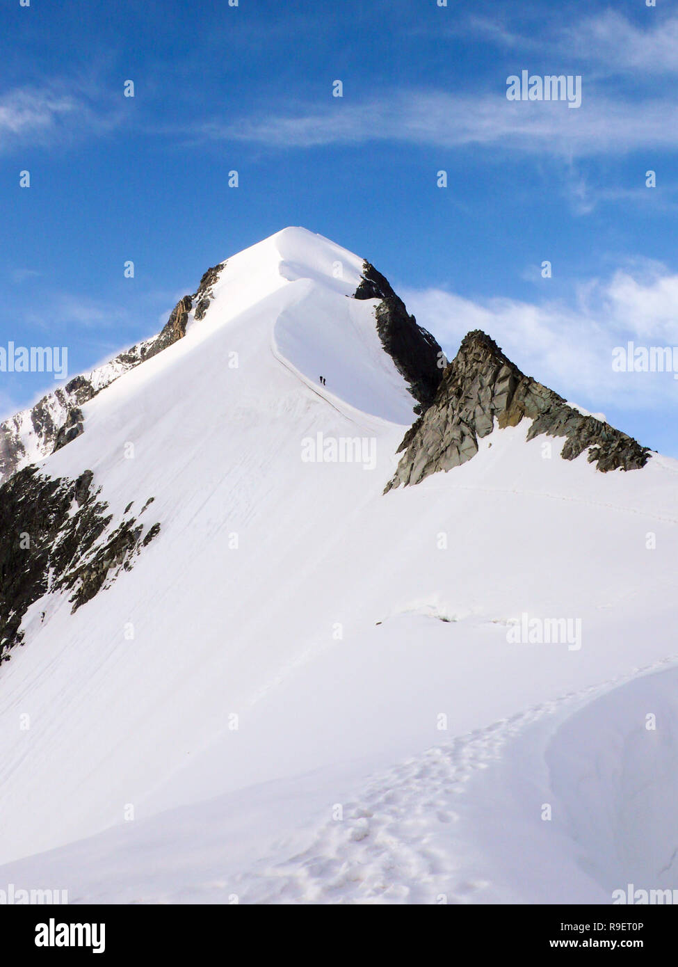 mountain climbers on a steep and narrow snow ridge leading to a high ...