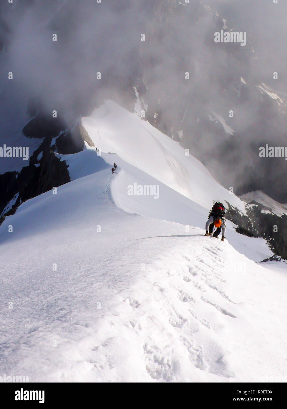 mountain climbers on a steep and narrow snow ridge leading to a high ...