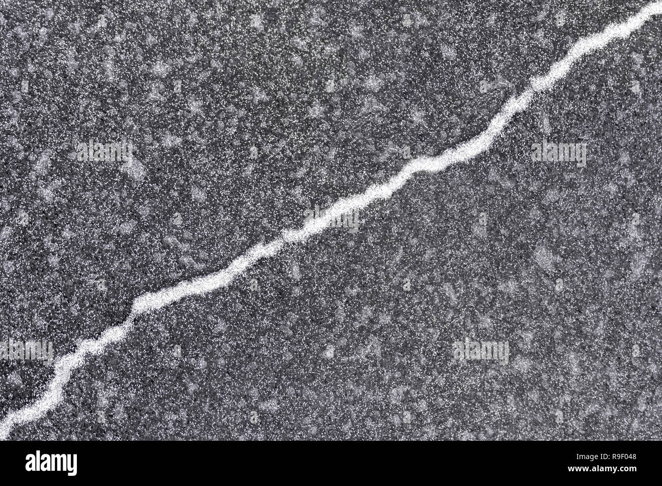 The crack on the gray ice powdered with snow and running diagonally ...