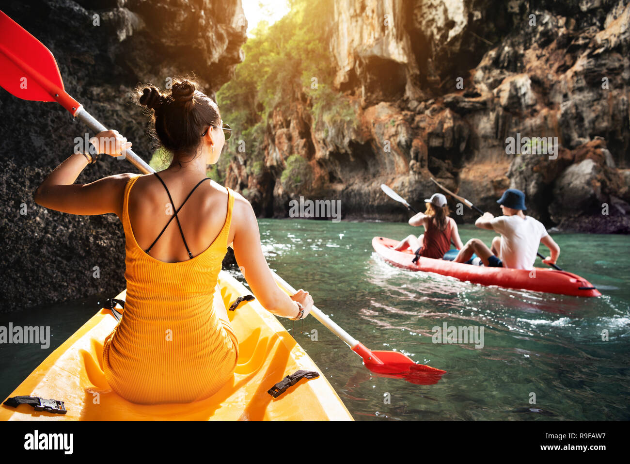 Beautiful lady and friends walks by kayaks at sea bay between big rocks ...