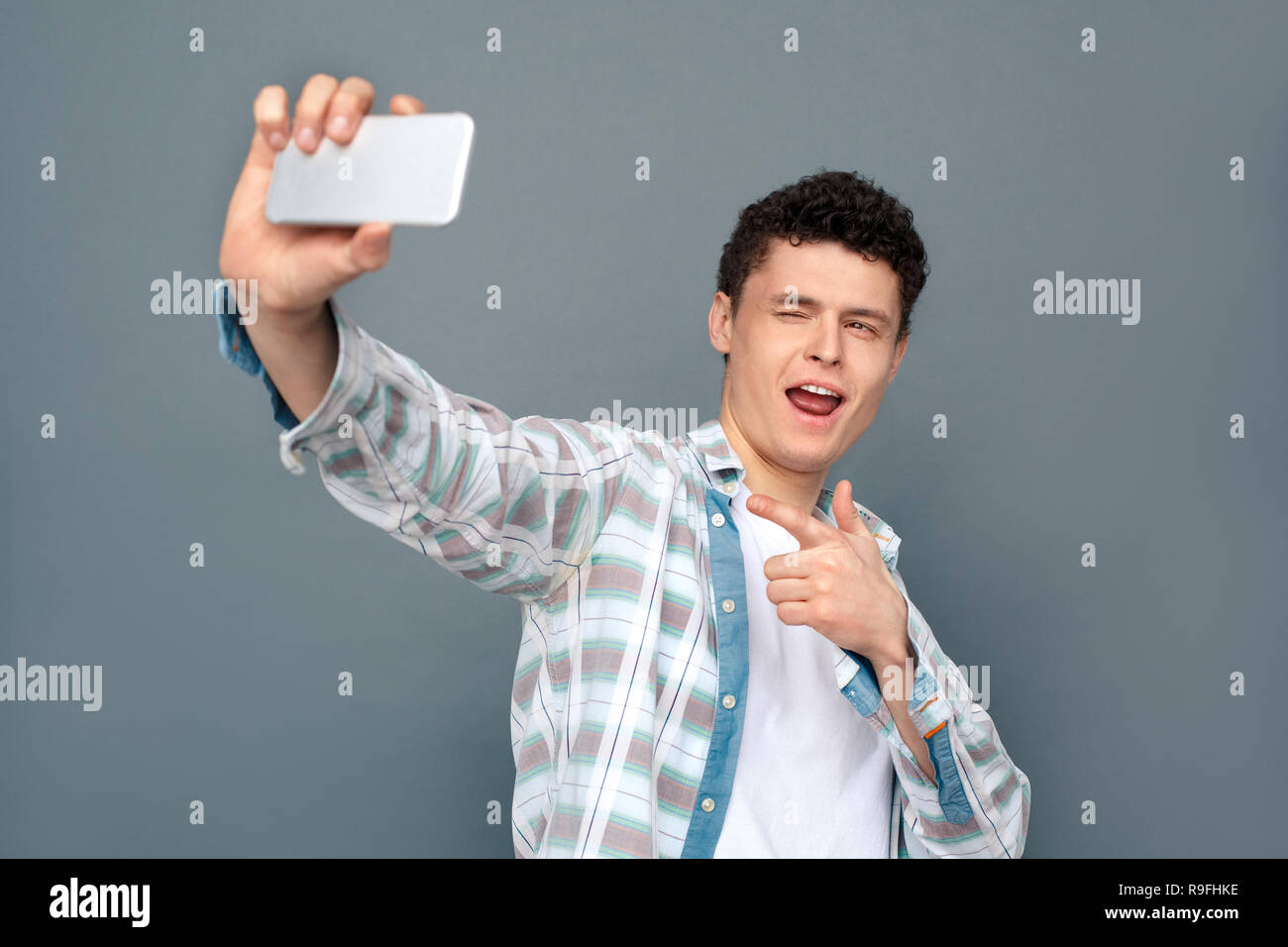 Young guy isolated on gray wall free style standing holding smartphone ...