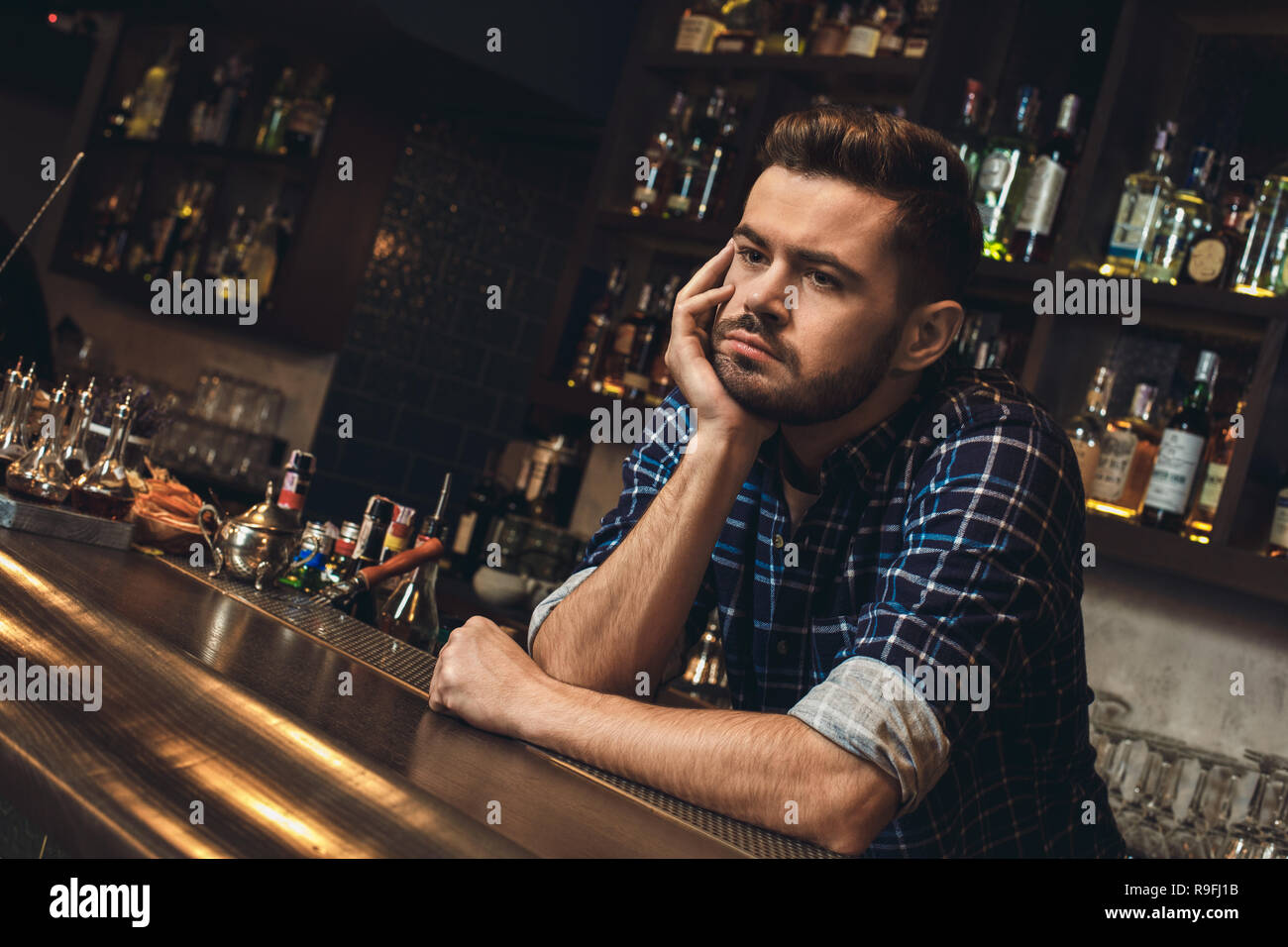 Young barman standing leaning on bar counter looking aside bored close ...