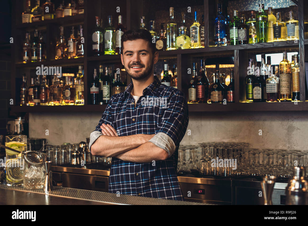 Young barman standing at bar counter crossed arms looking camera ...