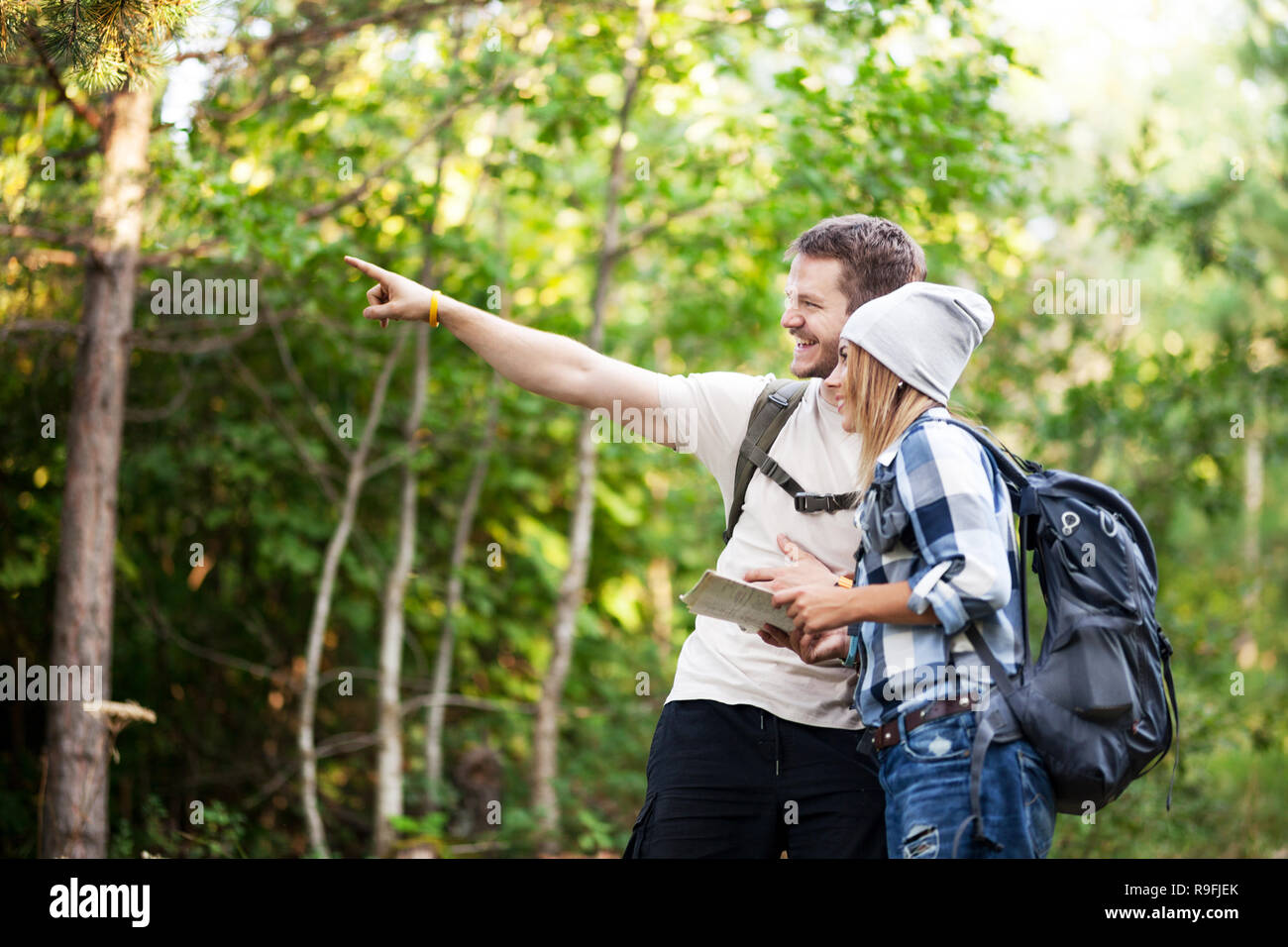 pretty couple hiking in a forest, looking at a map and pointing with ...