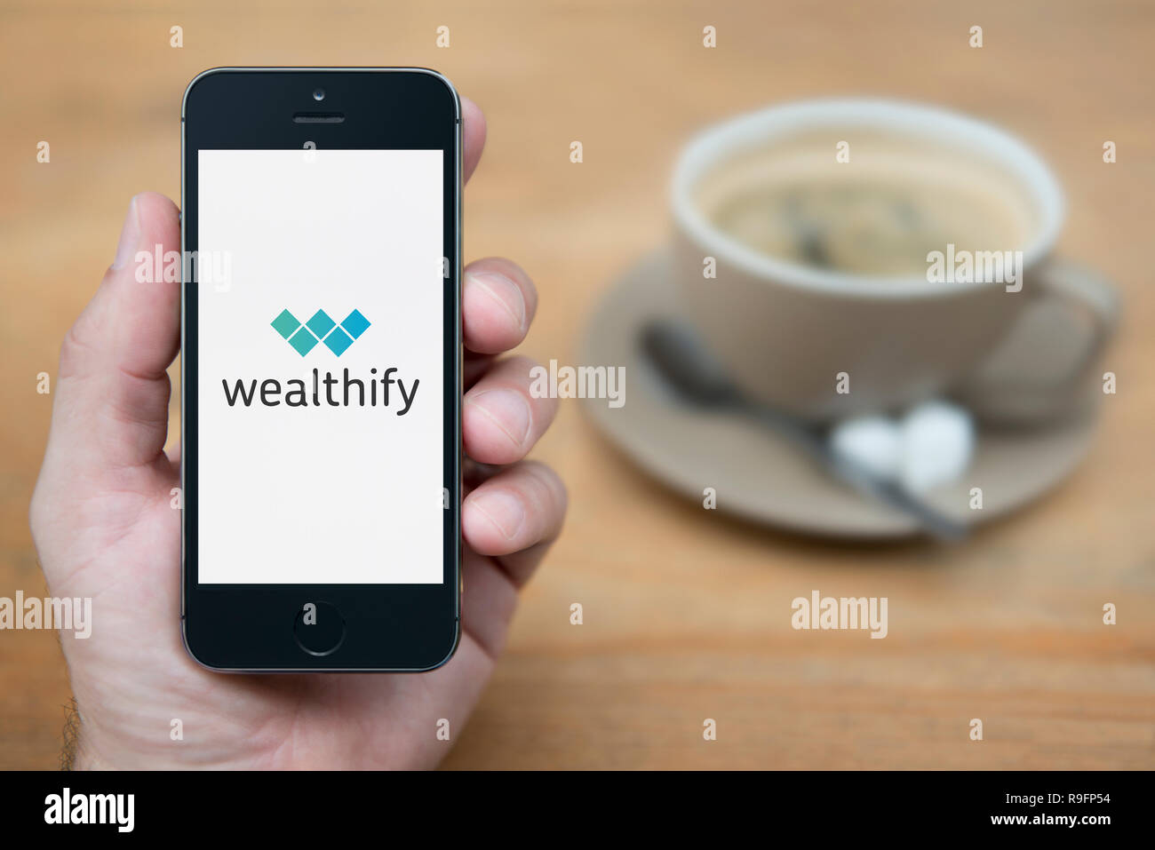 A man looks at his iPhone which displays the Wealthify logo (Editorial ...