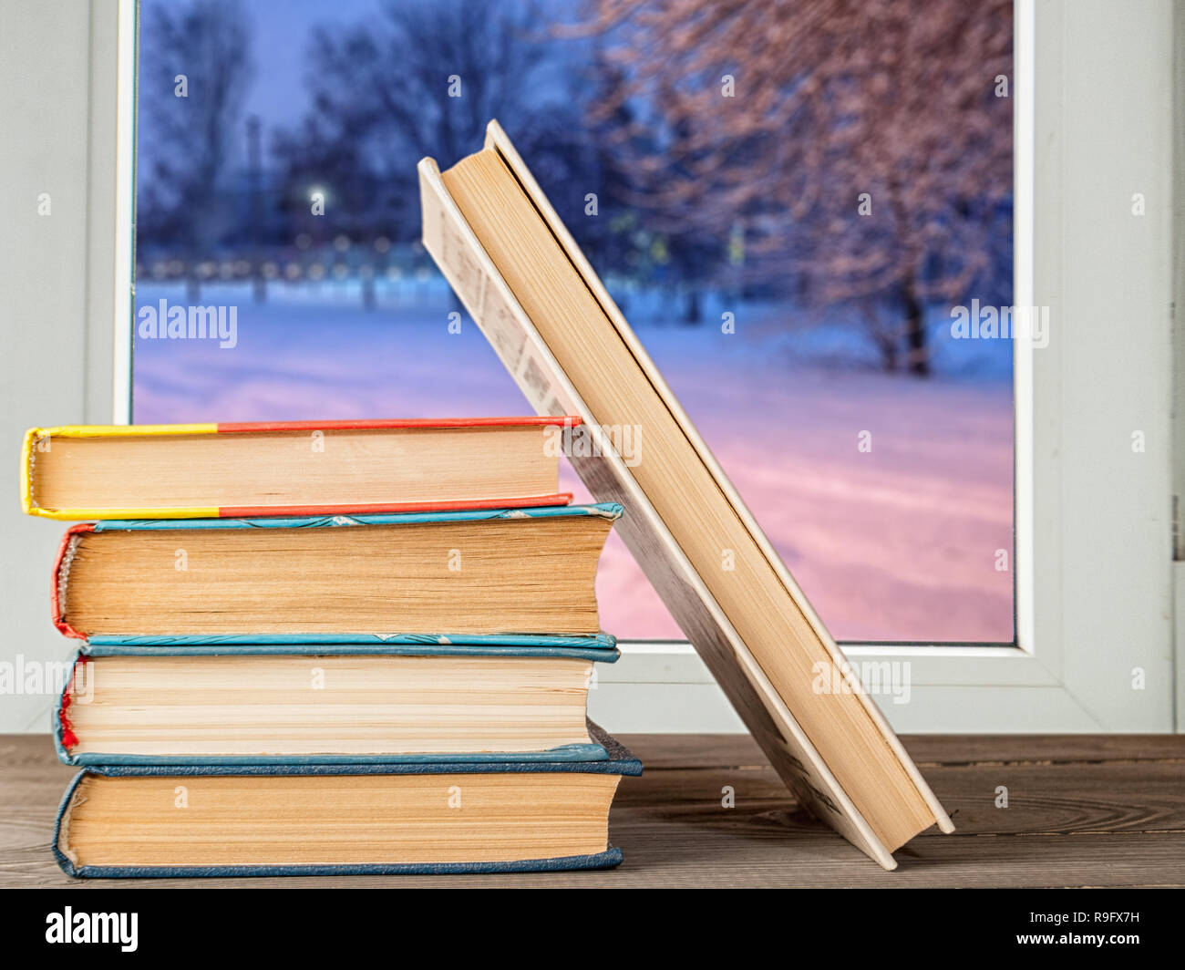 books on the desk against the window with a winter landscape at sunrise ...