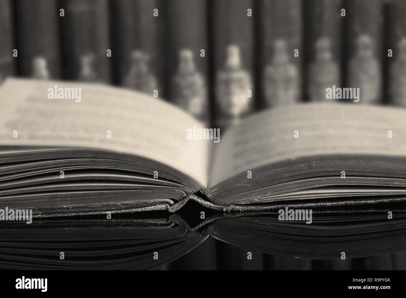 Book collection with an open book reflected on a black glass background ...