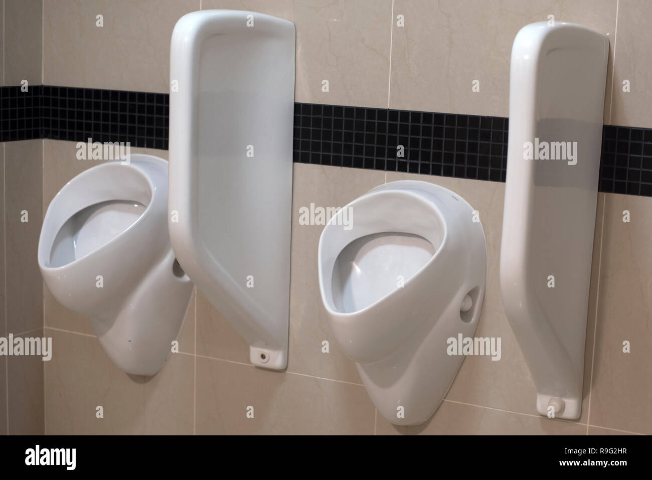 two white urinals in a public toilet separated by a partition and ...