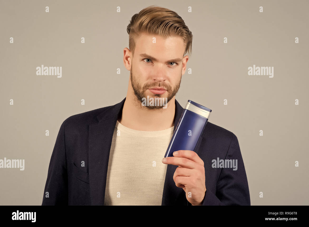 Man with shampoo or conditioner bottle in black jacket on grey ...