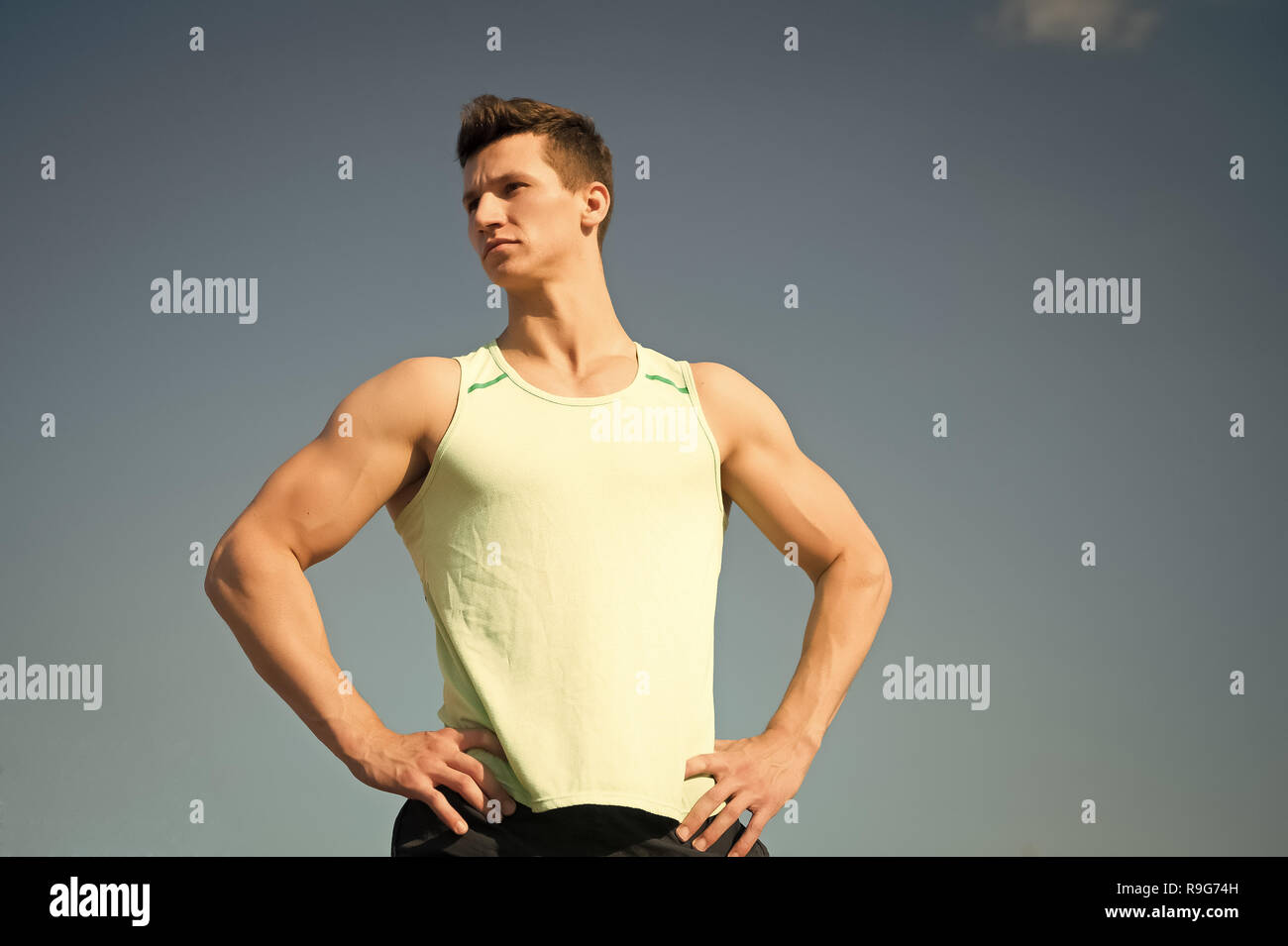 Man bodybuilder posing on blue sky. Athlete in green tshirt on sunny ...