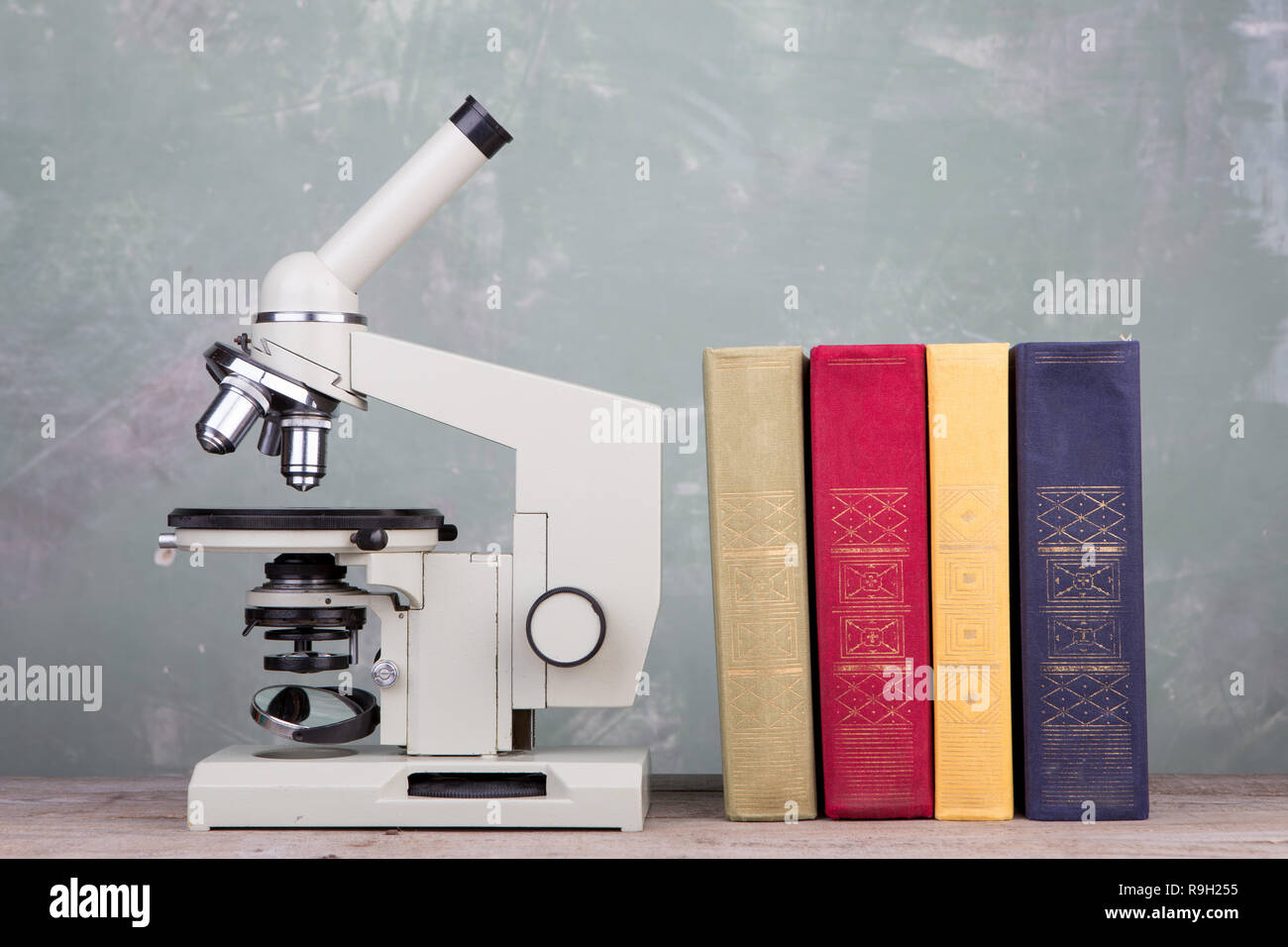 Education concept - books and microscope on the desk on green ...