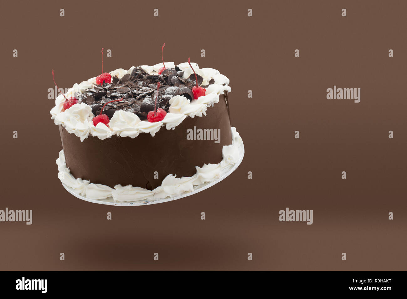 Chocolate cake with cream and cherries floating above brown background ...