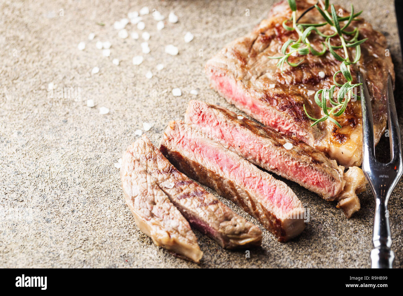 Sliced medium rare grilled beef steak with rosemary and spices on dark ...