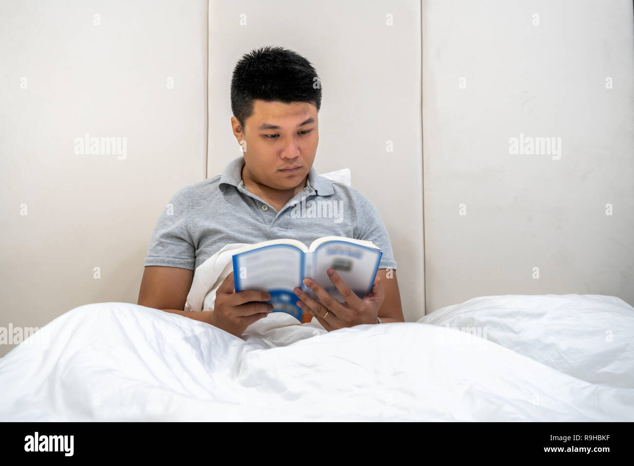 Asian man reading book on white bed Stock Photo - Alamy