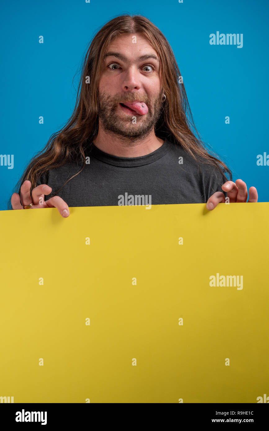 Male portrait making funny grimace while holding a yellow advertise ...