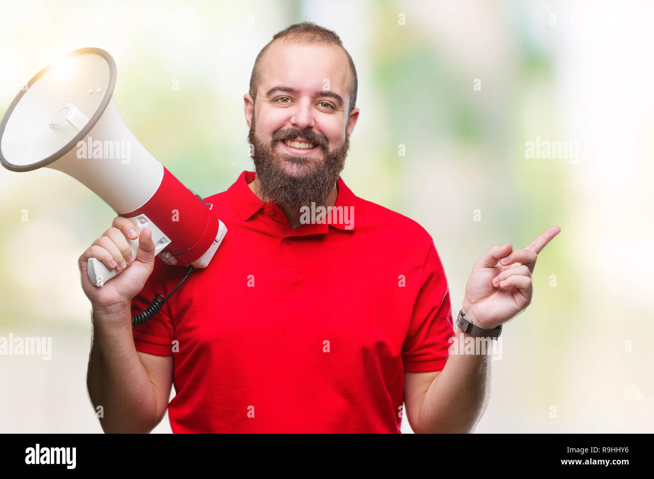 Young caucasian man shouting through megaphone over isolated background ...