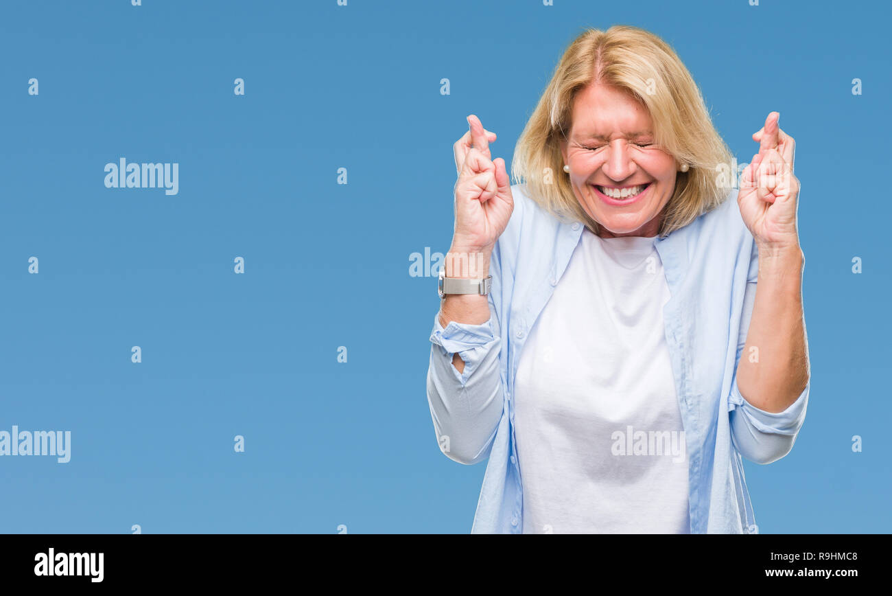 Middle age blonde woman over isolated background smiling crossing fingers with hope and eyes ...