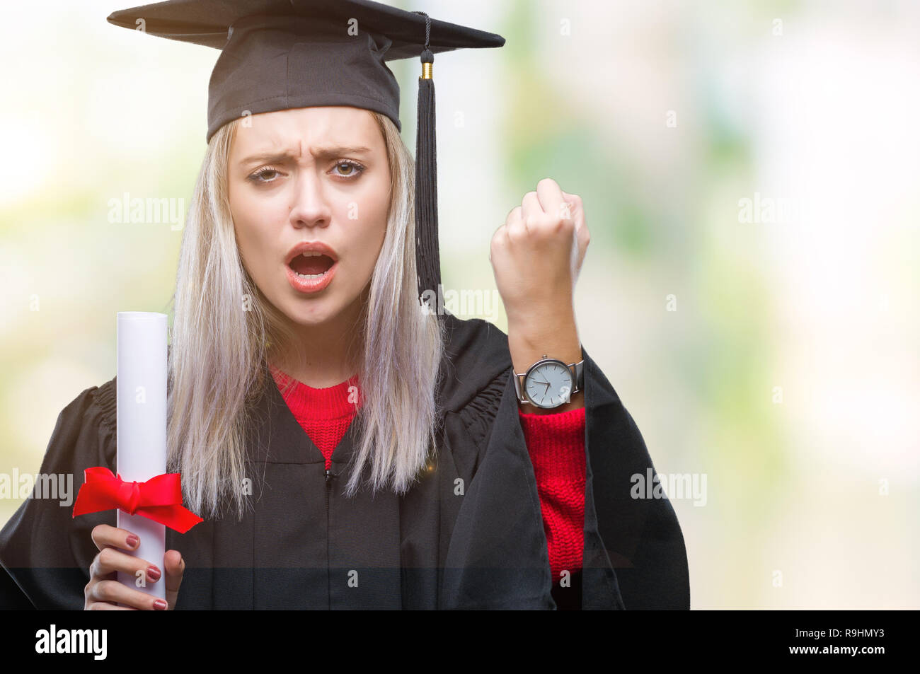 Young blonde woman wearing graduate uniform holding degree over ...