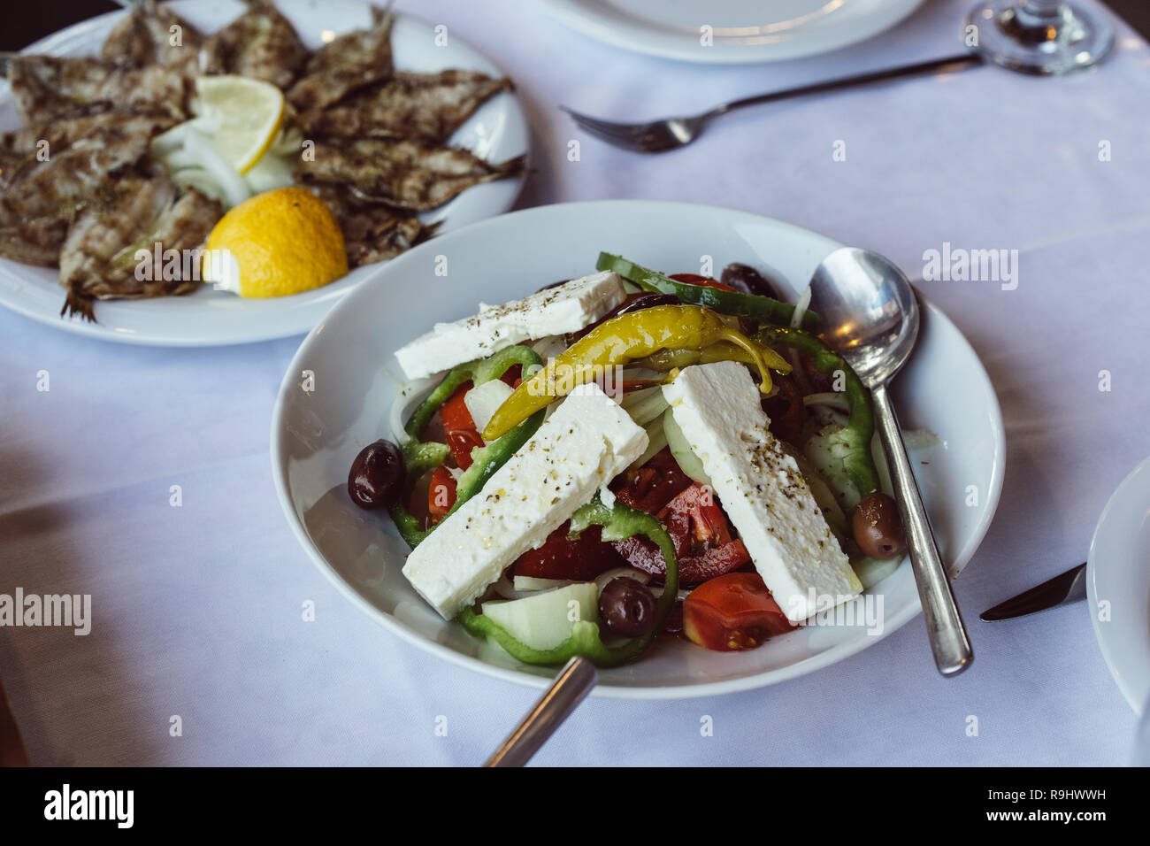 Small fried fish with lemon and Greek salad Stock Photo - Alamy