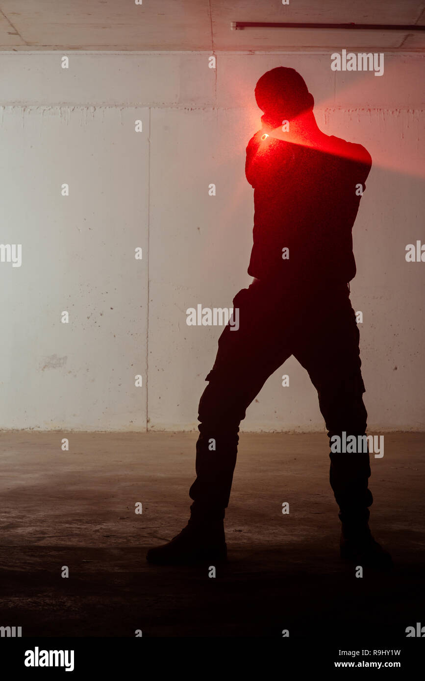 A man is standing in a dark room and holding laser gun in his hands ...