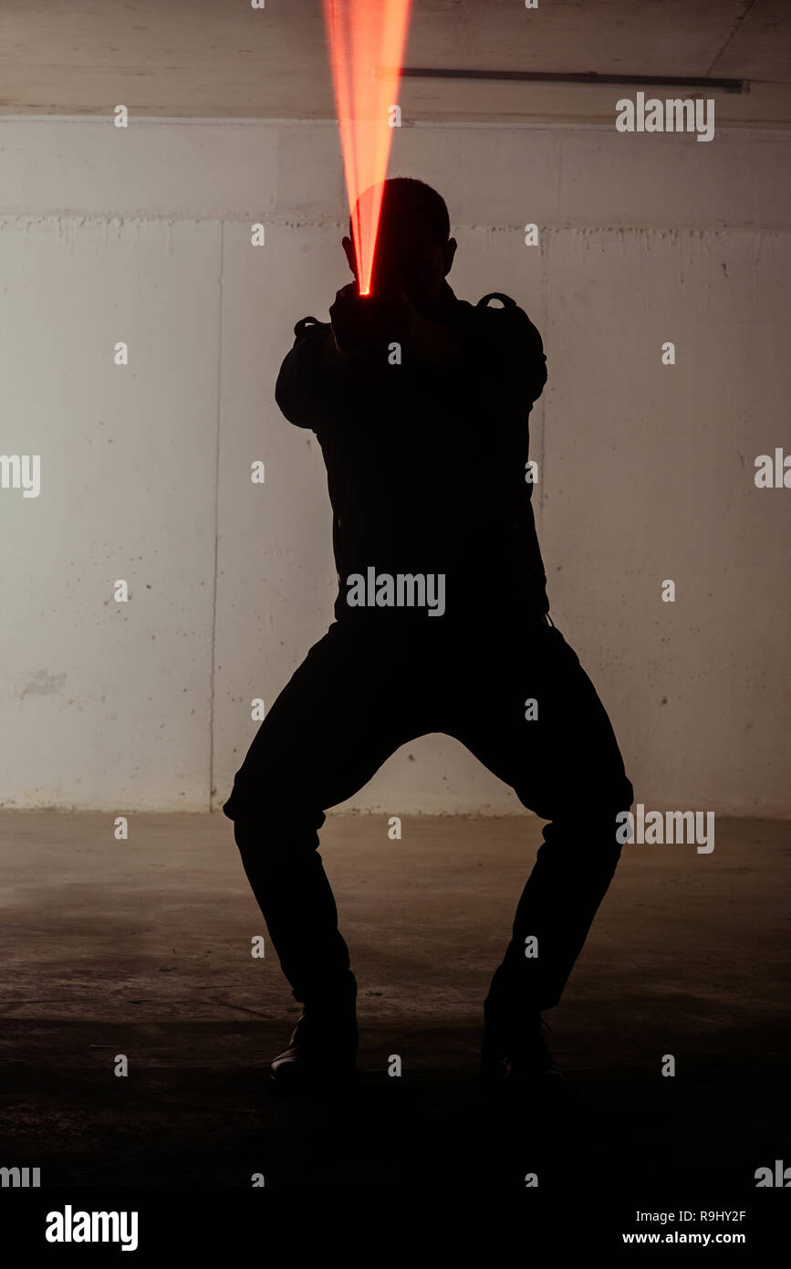 Assassin man is standing in a dark room and holding laser gun in his ...