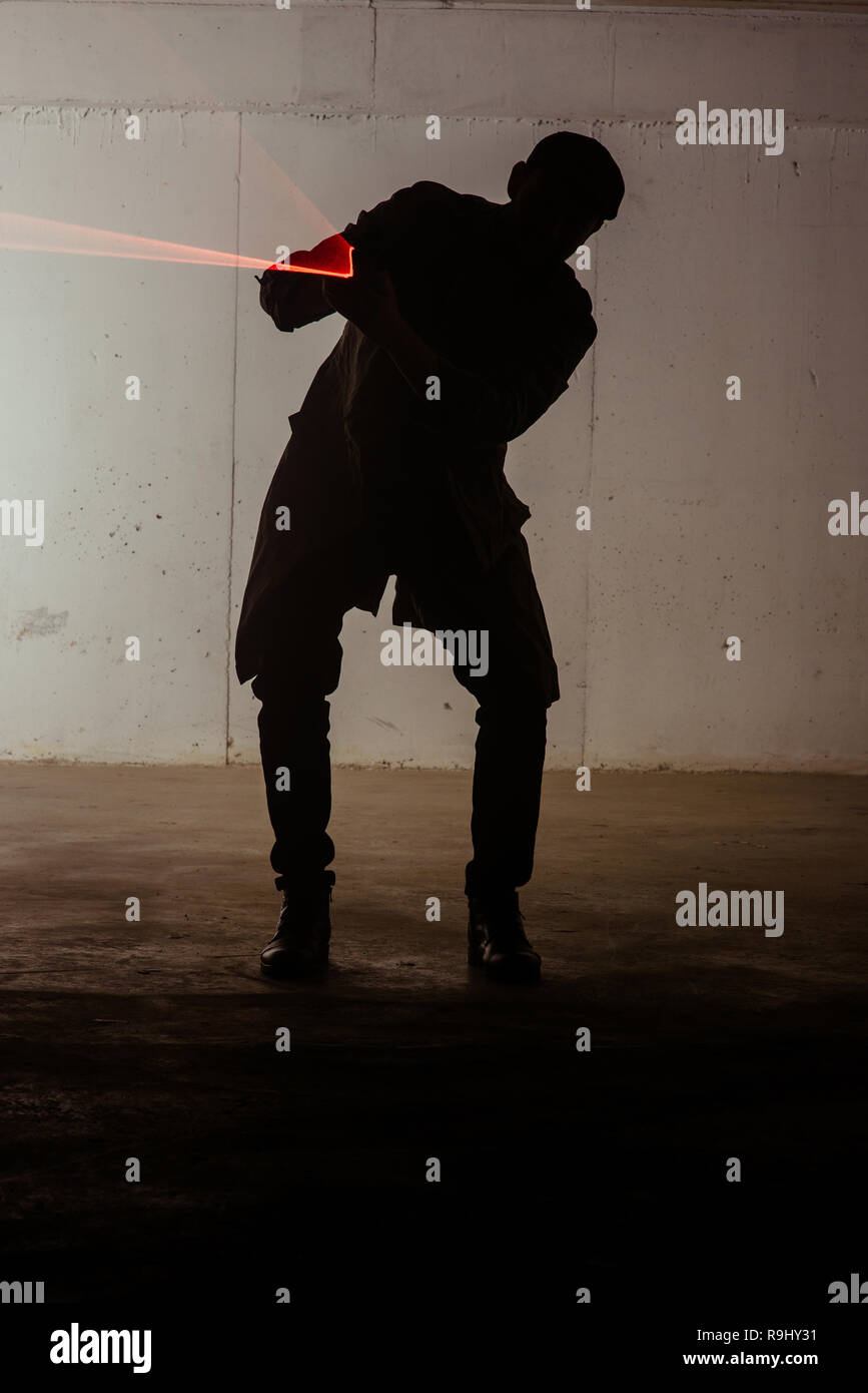 A man is standing in a dark room and holding laser gun in his hands ...