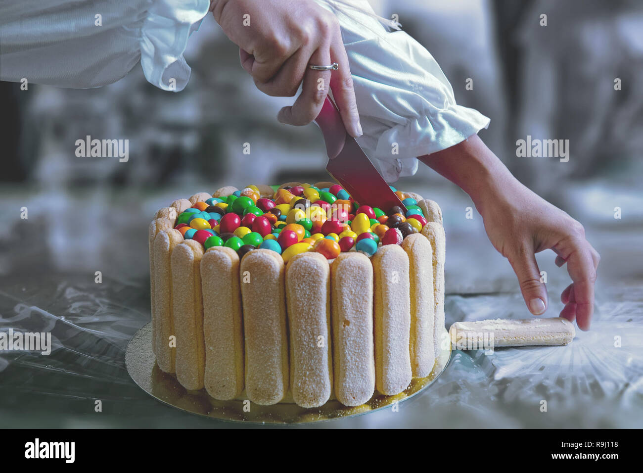 Female hands cut a cake with a lot of colored round chocolates at a ...