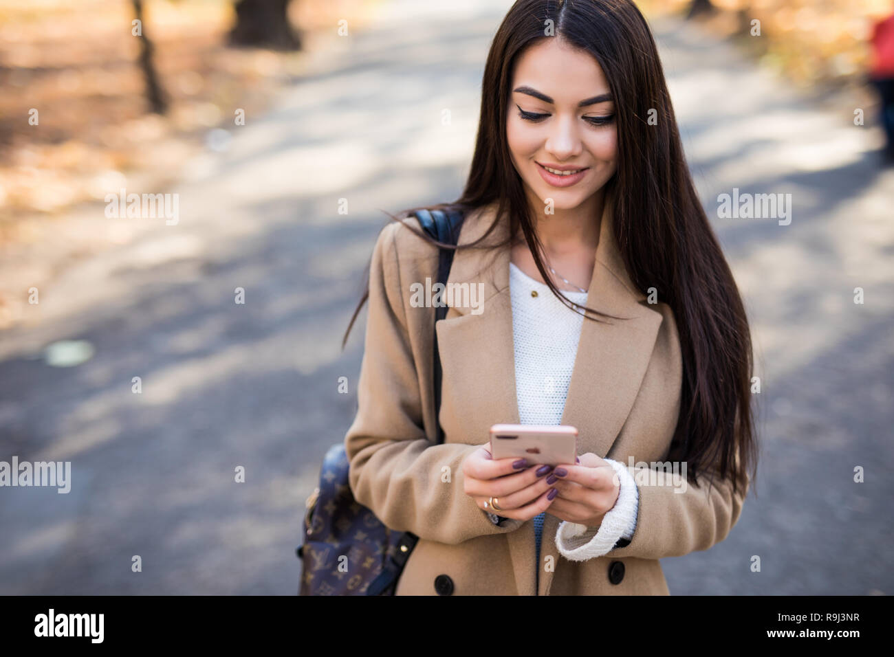 Beautiful woman dressed in autumn coat outdoors, drinking coffee, using ...