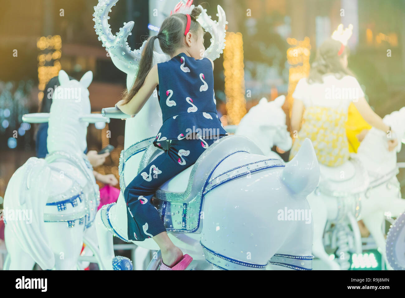 Adorable Asian little kid girl riding on a merry go round carousel ...