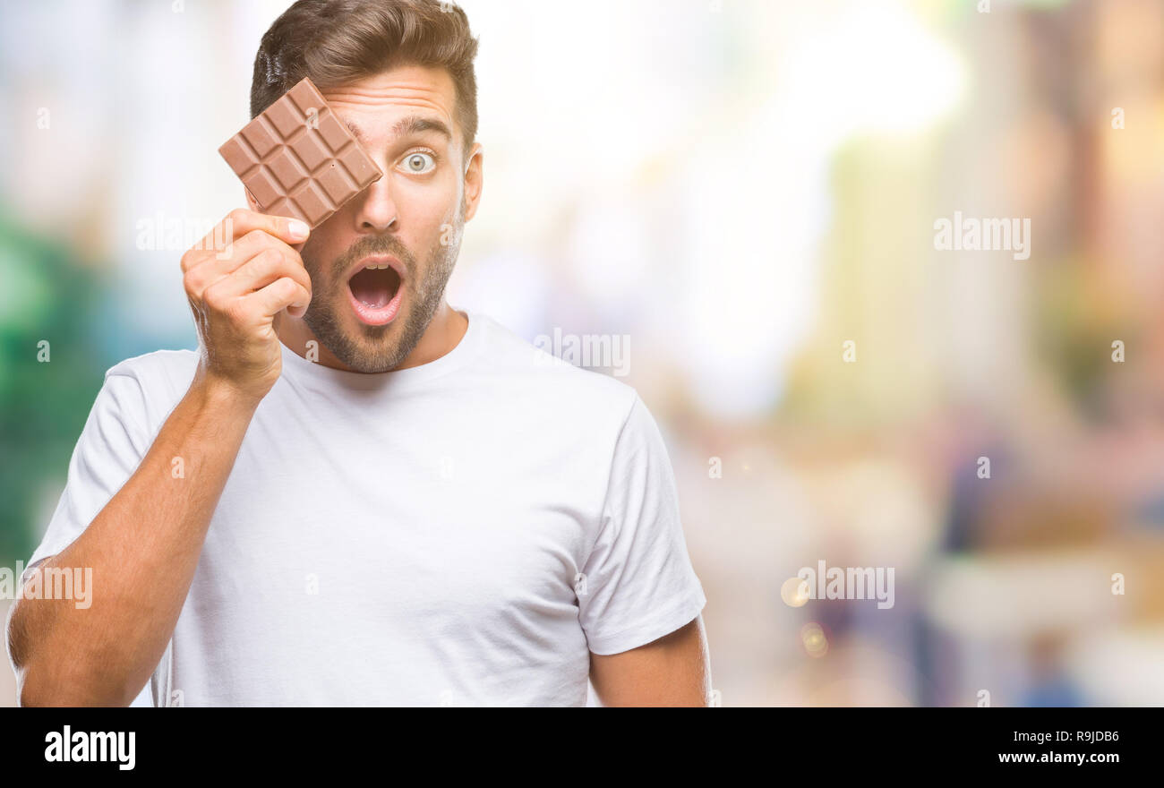 Young handsome man eating chocolate bar over isolated background scared ...