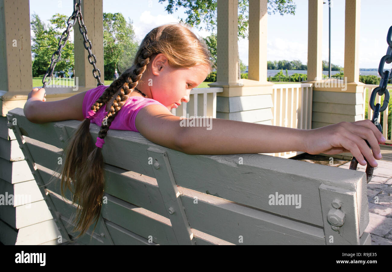 Sad, dreamy looking girl sitting on swing bench in the park Stock Photo ...