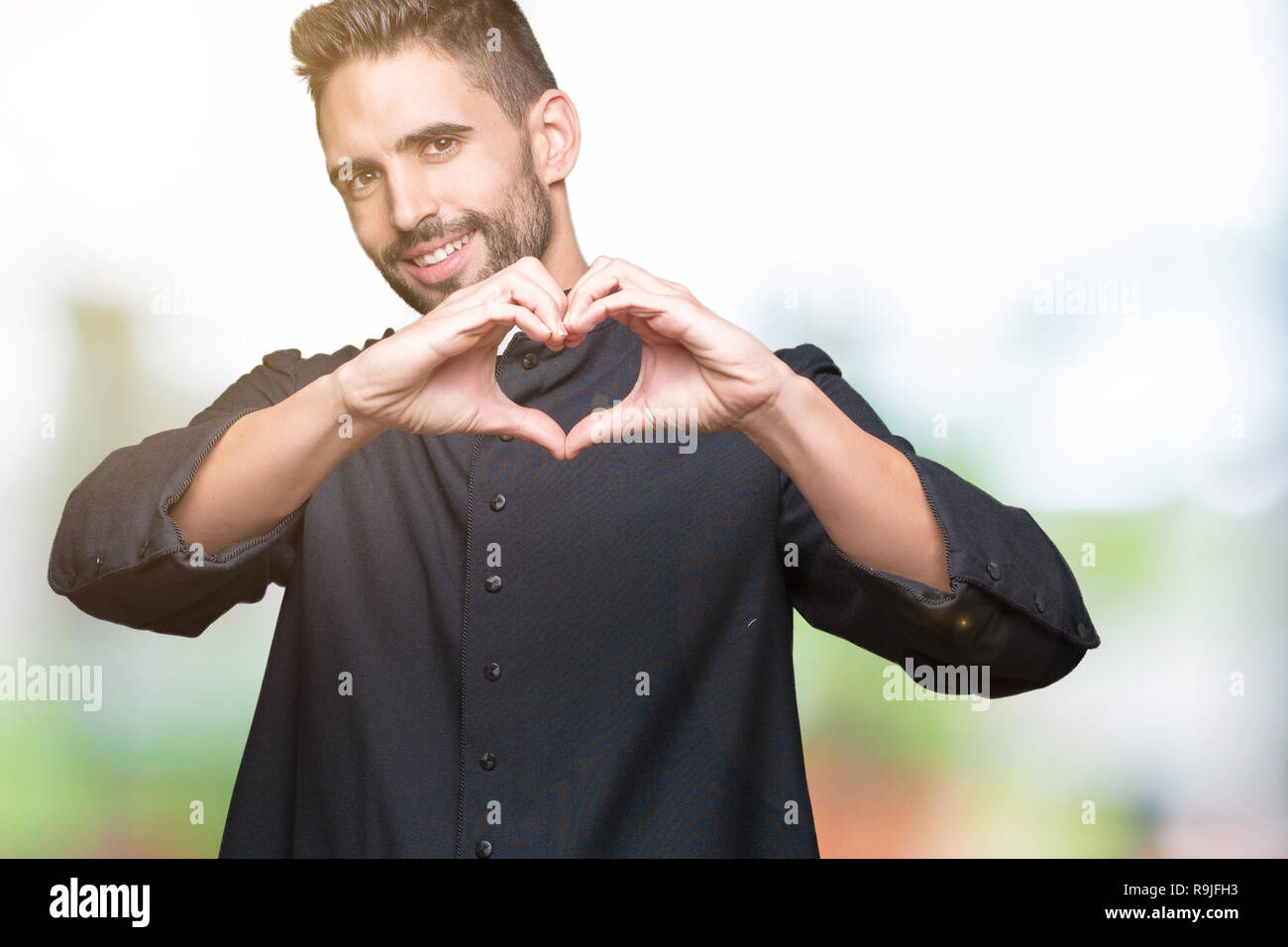 Young Christian priest over isolated background smiling in love showing ...