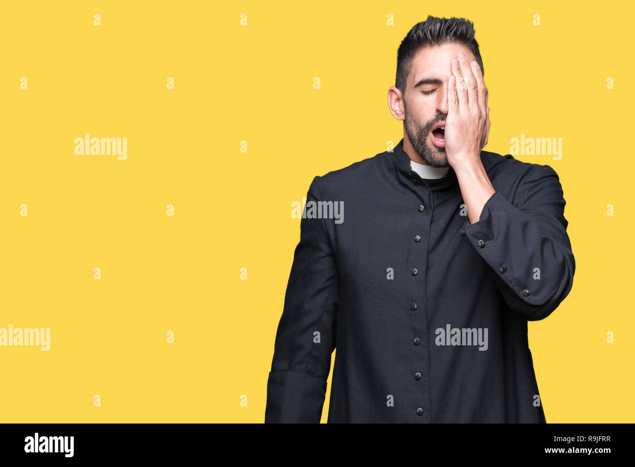 Young Christian priest over isolated background Yawning tired covering ...