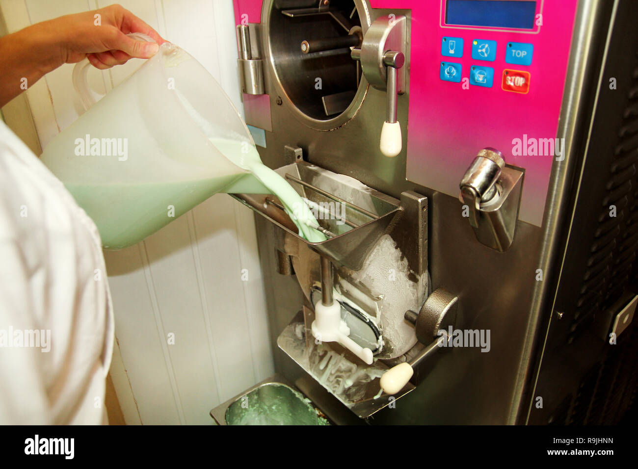 Female chef at ice cream factory is pouring mixed basic ingredients ...