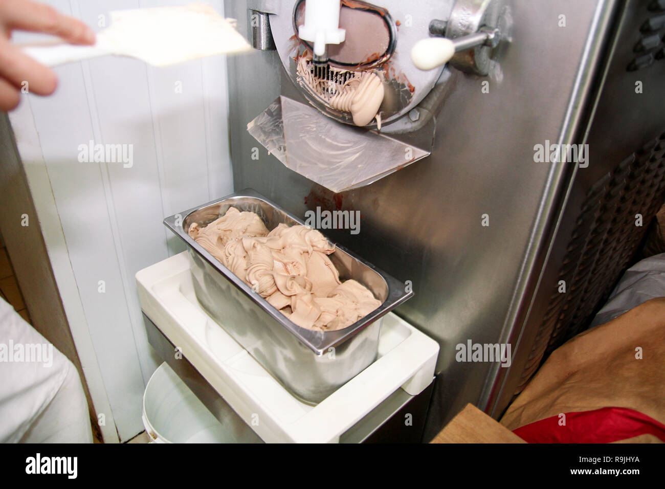 Confectioner in chef uniform is working on ice cream maker machine ...