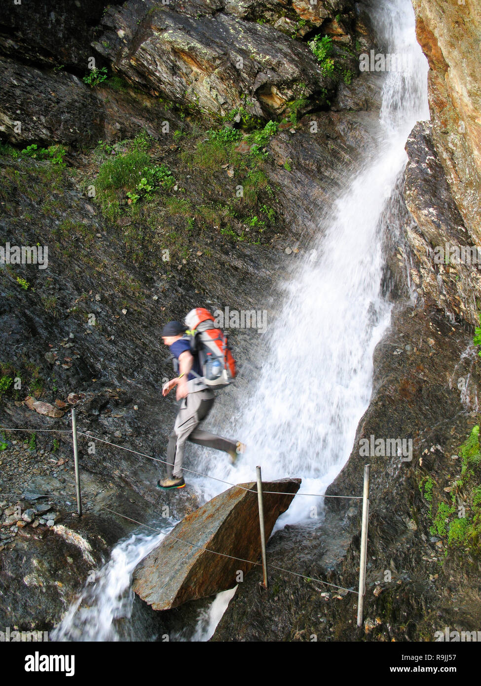 mountain climber hiking under a waterfall on a rocky hiking trail and ...