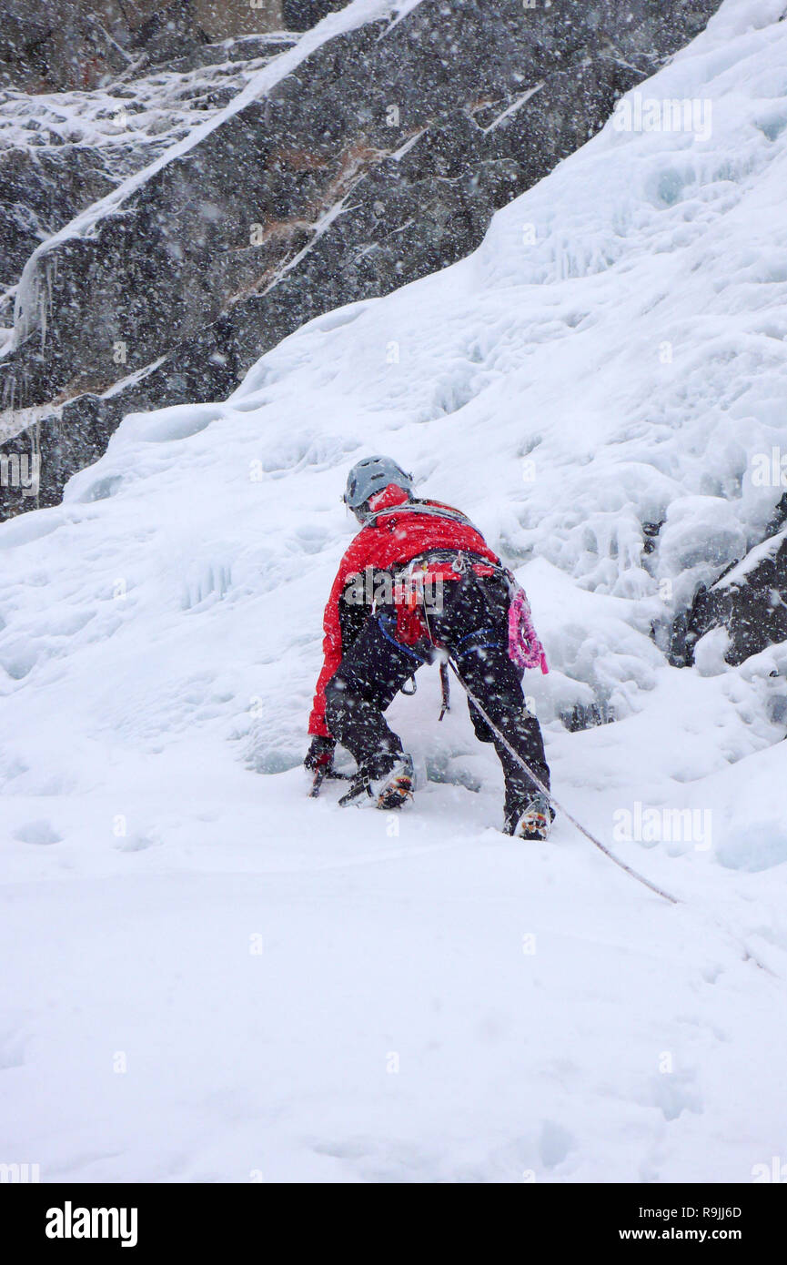 male ice climber in heavy snowfall and bad weather climbing a frozen ...