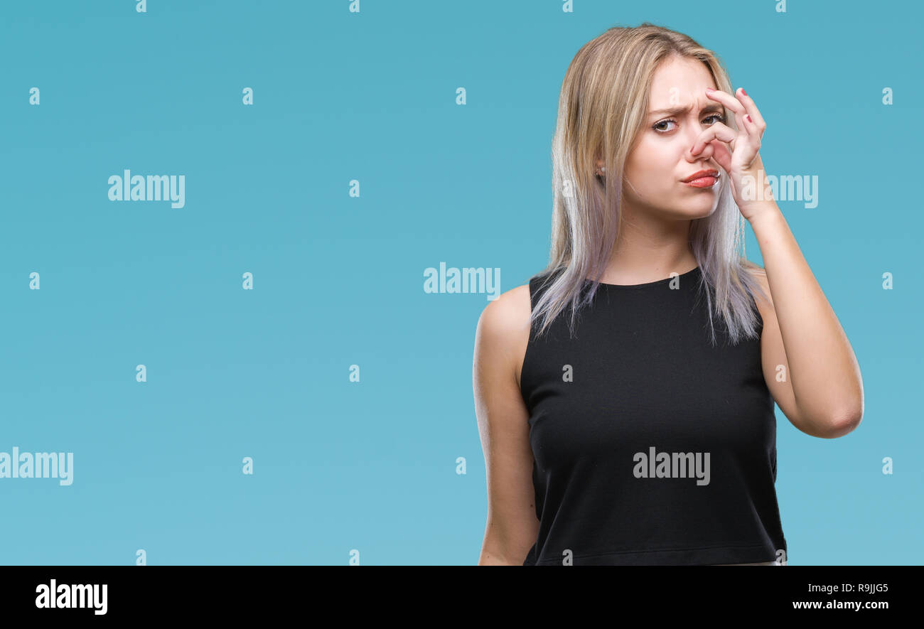 Young blonde woman over isolated background smelling something stinky ...