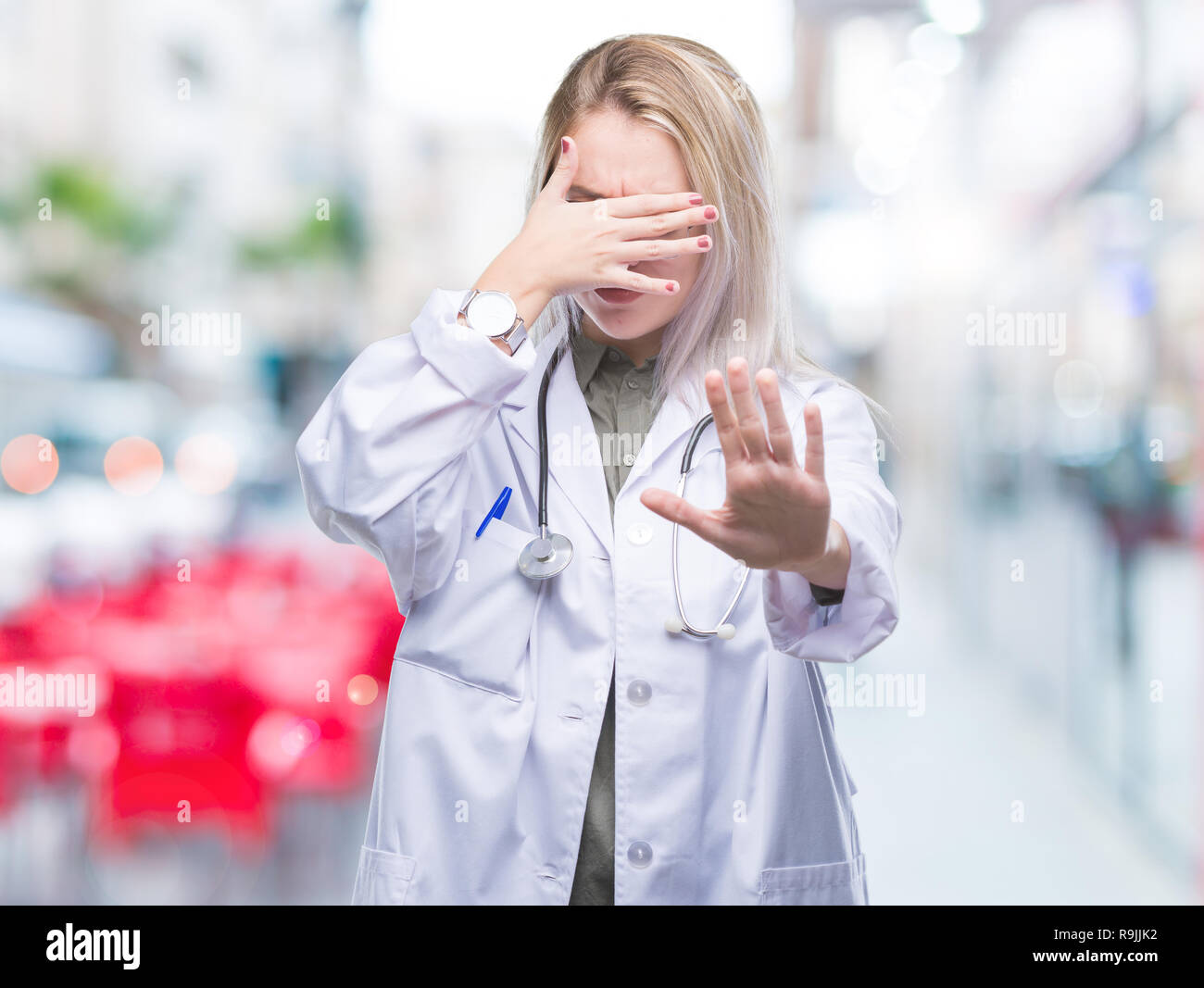 Young blonde doctor woman over isolated background covering eyes with ...