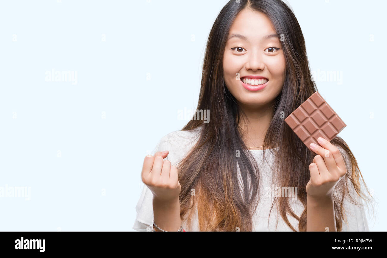 Young asian woman eating chocolate bar over isolated background ...