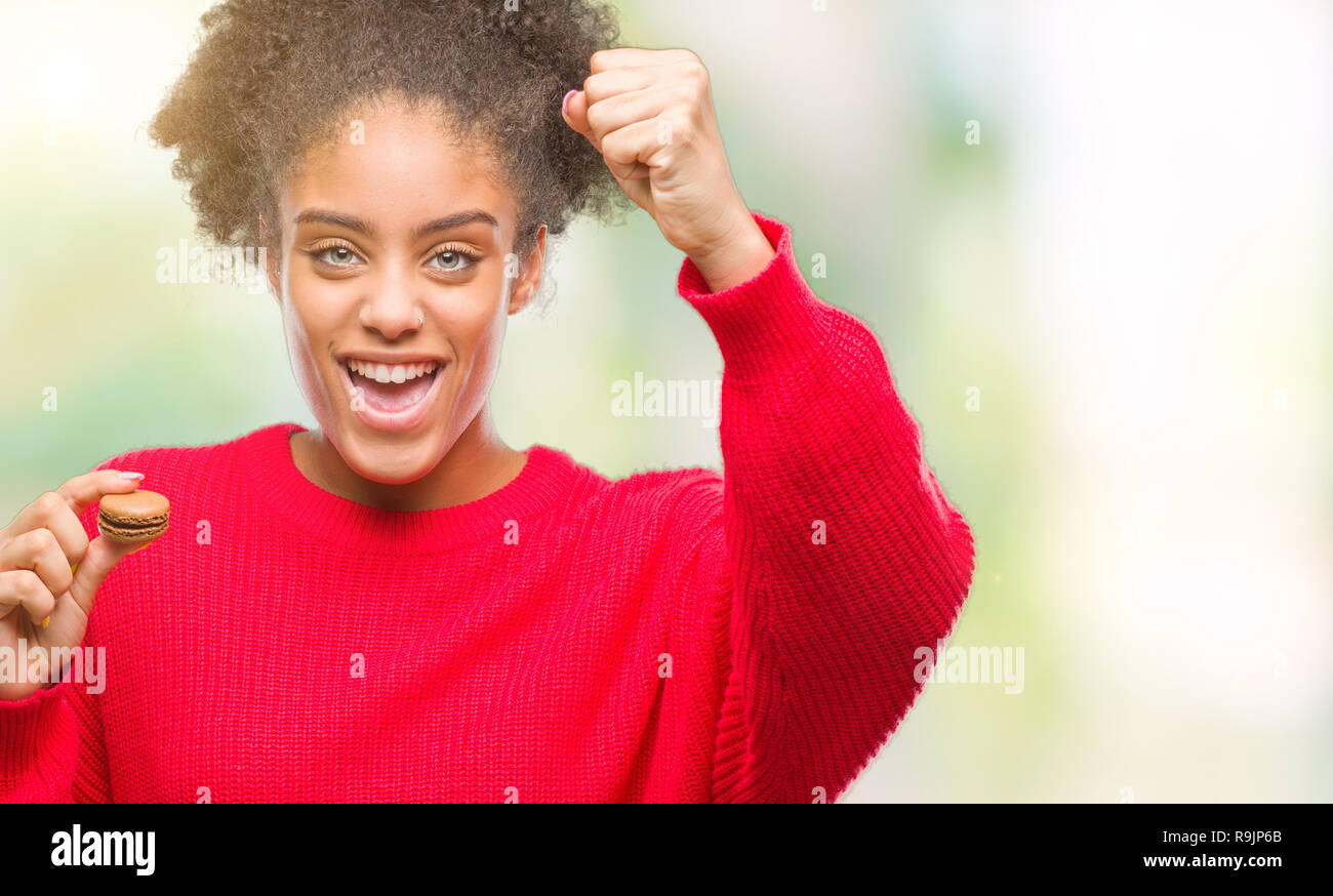Young afro american woman eating chocolate macaron over isolated ...