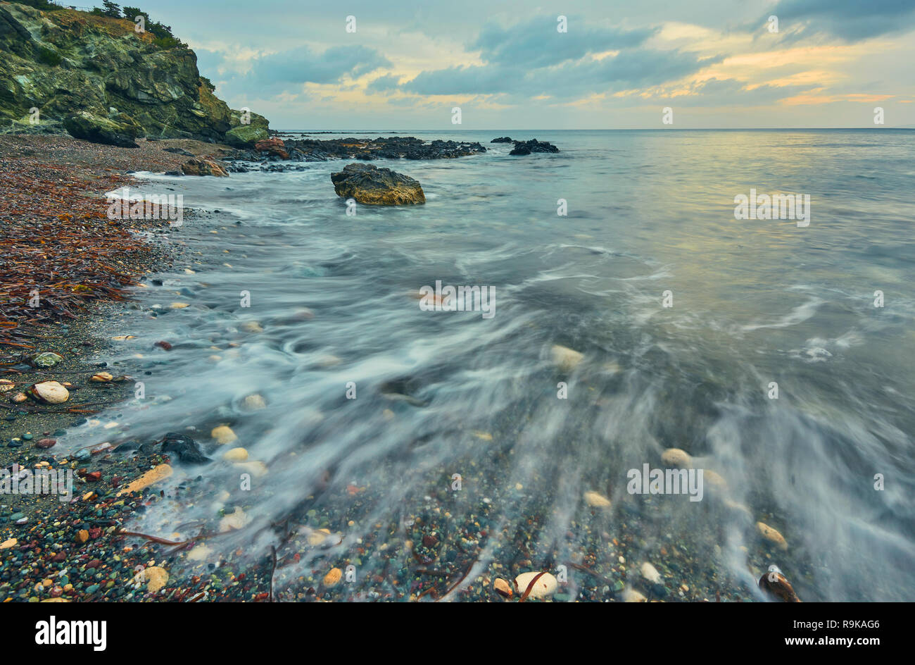 Stones and rocks in forefront with creamy surf ebbing and flowing on ...